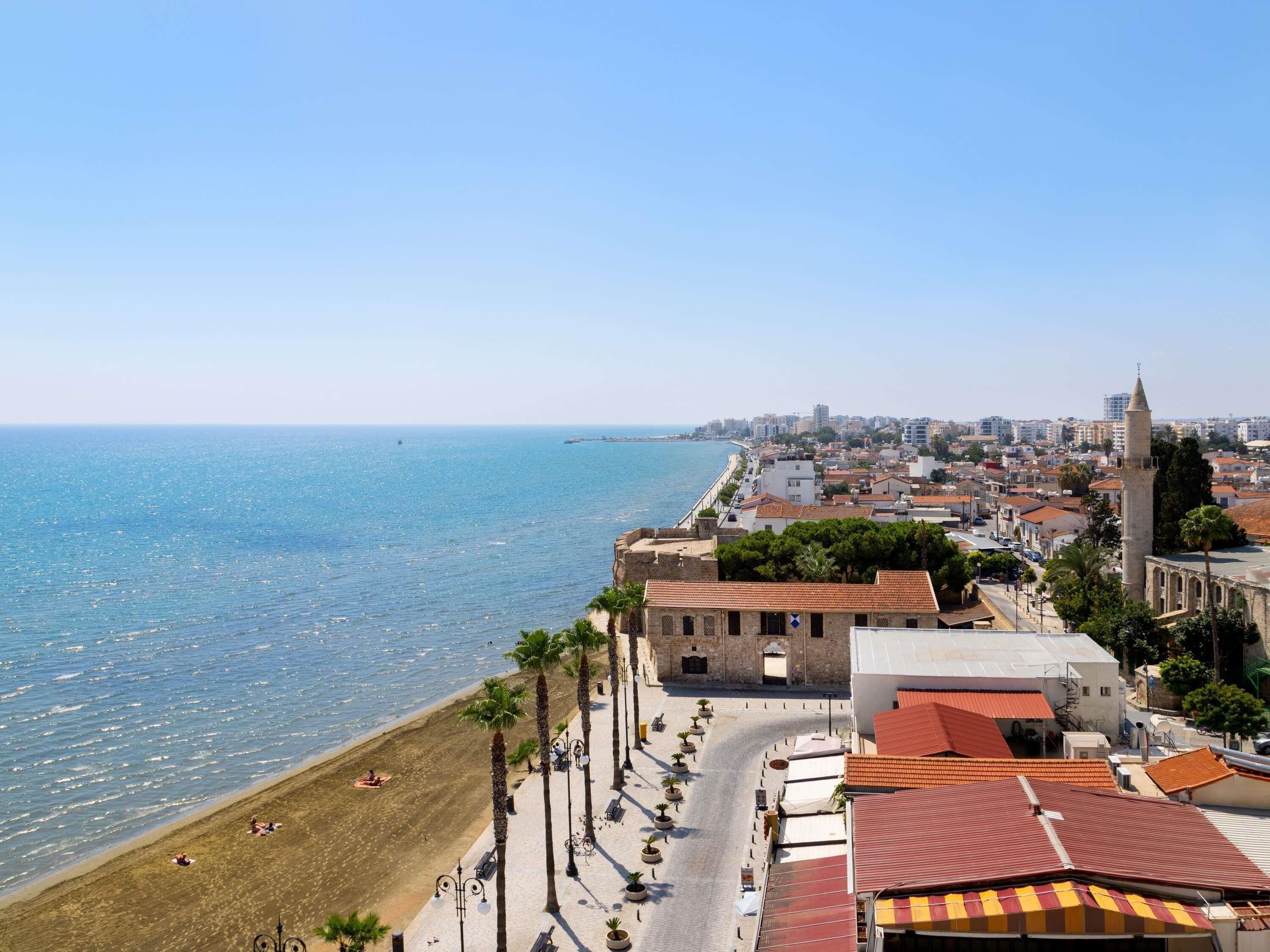 Paisagem costeira com praia, edifícios e uma torre imponente.