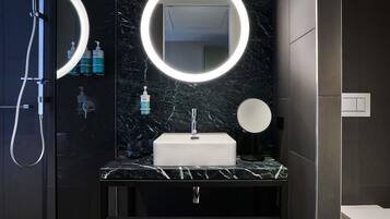 Casa de banho moderna com bancada de mármore, lavatório embutido, chuveiro manual e dois espelhos fixados na parede com iluminação integrada.
