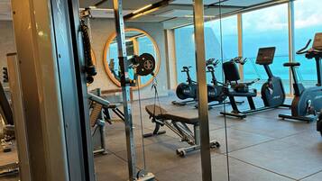 Uma academia com equipamentos de ginástica, grandes janelas e vista para o céu.