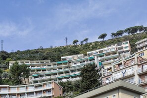 Um edifício residencial de vários andares com varandas, localizado numa encosta arborizada.