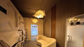 Um corredor com uma cadeira branca curvada, uma parede branca com uma porta e um luminário no teto.