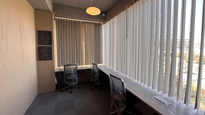 Uma sala de conferência com uma mesa comprida, duas cadeiras, uma luminária no teto e uma janela com venezianas verticais.