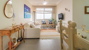 Uma sala de estar com sofá, mesa de madeira, televisão e canto de jantar com cadeiras e mesa.