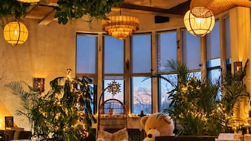 Um espaço interno aconchegante com plantas penduradas, luminárias de vime e um urso de pelúcia grande.