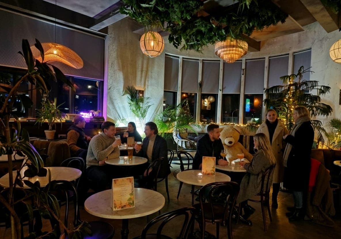 Espaço de refeições interno com mesas redondas, plantas penduradas e iluminação pendente.