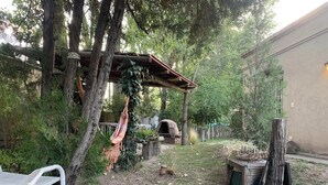Uma área externa rústica com uma pérgola de madeira, um forno de tijolos e uma rede.