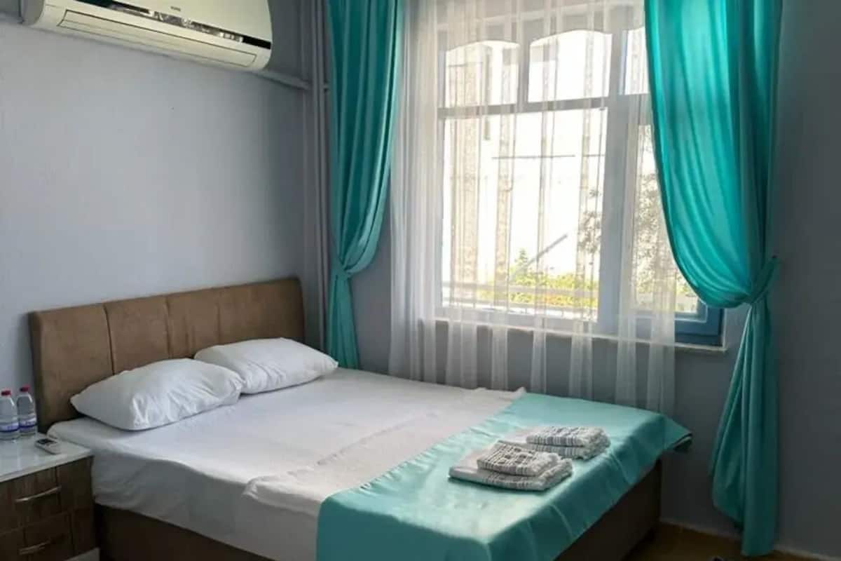 Uma cama bem arrumada com um cobre-leito azul-turquesa, almofadas brancas e uma toalha dobrada ao lado.