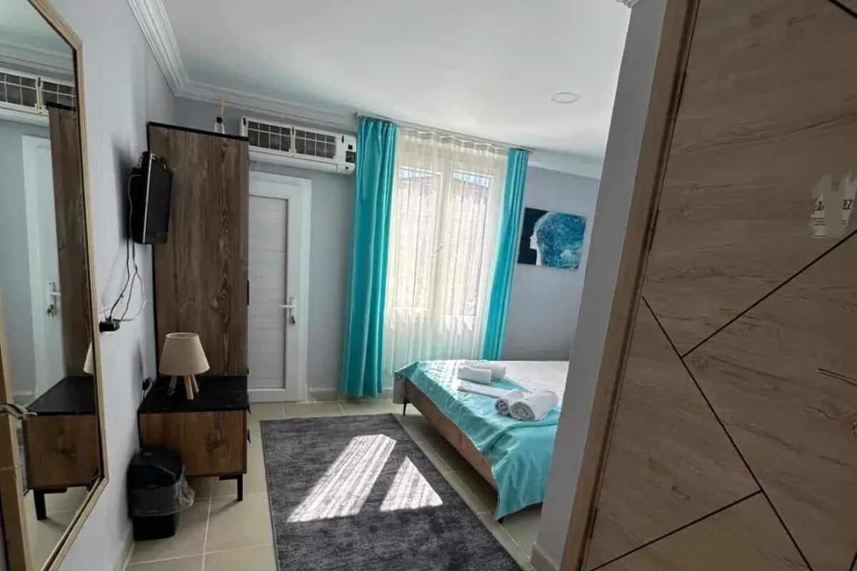 Um quarto com cama, cômoda, espelho, televisão e guarda-roupa.