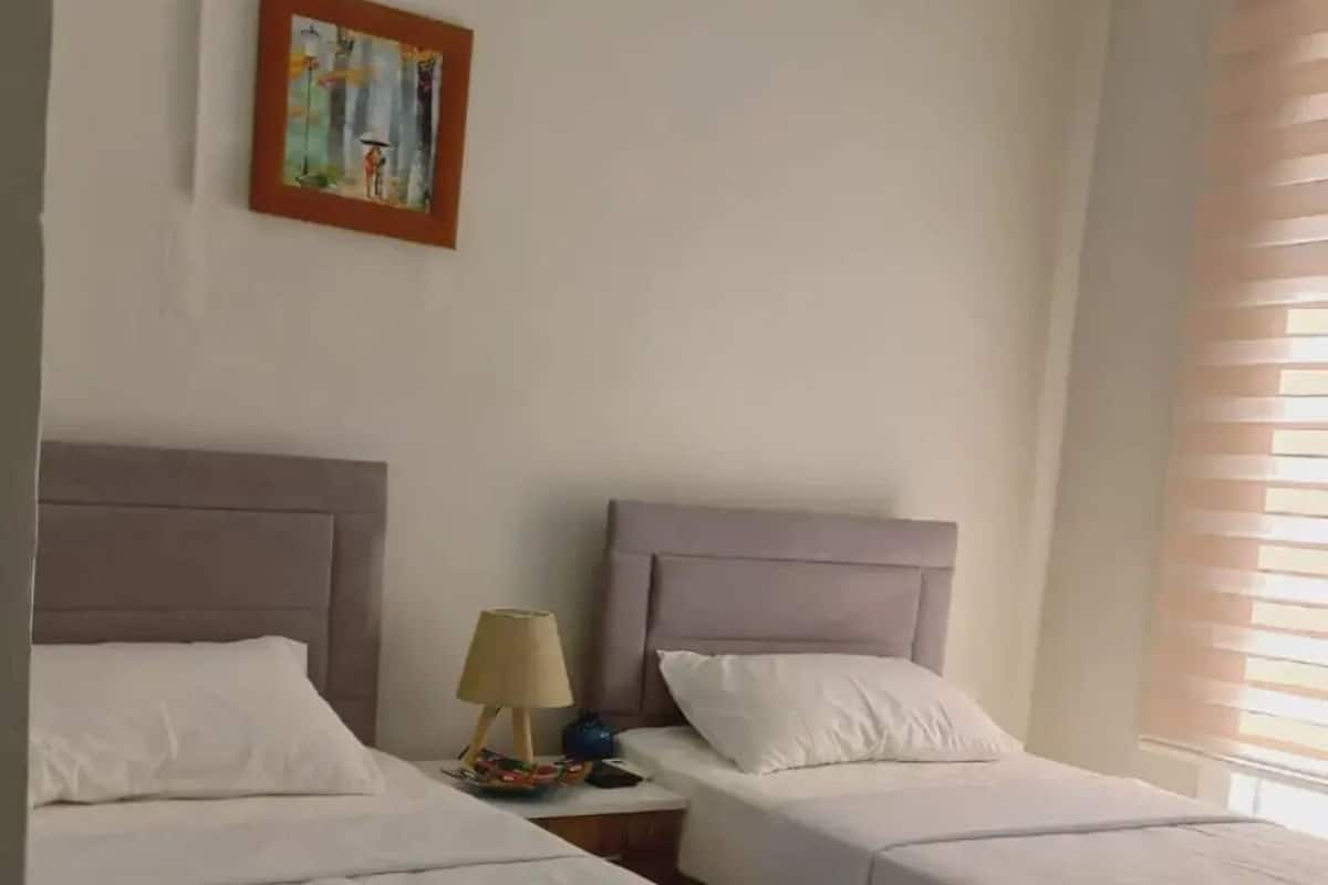 Quarto de hotel com duas camas, cada uma com cabeceira, mesa de cabeceira com abajur e um quadro na parede.