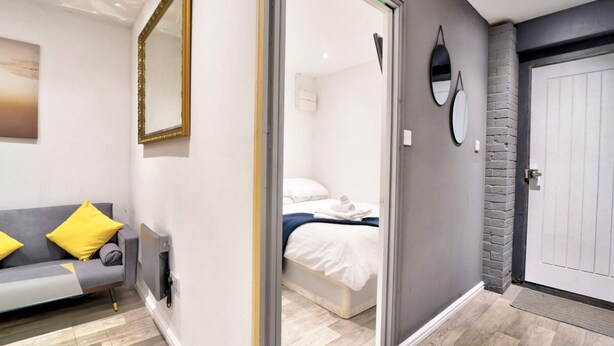 Quarto moderno com sofá cinza, cama com roupa de cama branca e parede de tijolos cinzas como destaque.