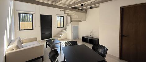 Uma sala moderna com sofá, mesa de jantar, cadeiras, escada e porta.