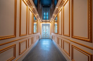 Um corredor com molduras douradas elaboradas, piso de azulejos e uma porta dupla no final.