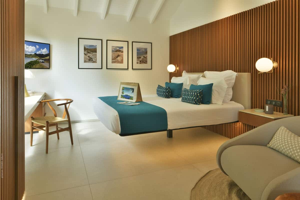 Quarto moderno com cama, mesas de cabeceira, escrivaninha e cadeira. Há quadros nas paredes e uma luminária na mesa de cabeceira.