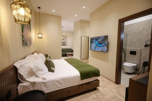 Quarto moderno com uma cama grande, manta verde e cabeceira de madeira. Há uma pintura na parede e um lustre no teto.