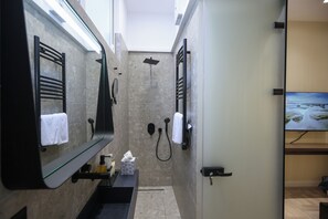 Casa de banho moderna com cabine de chuveiro em vidro, porta-toalhas e televisão na parede.