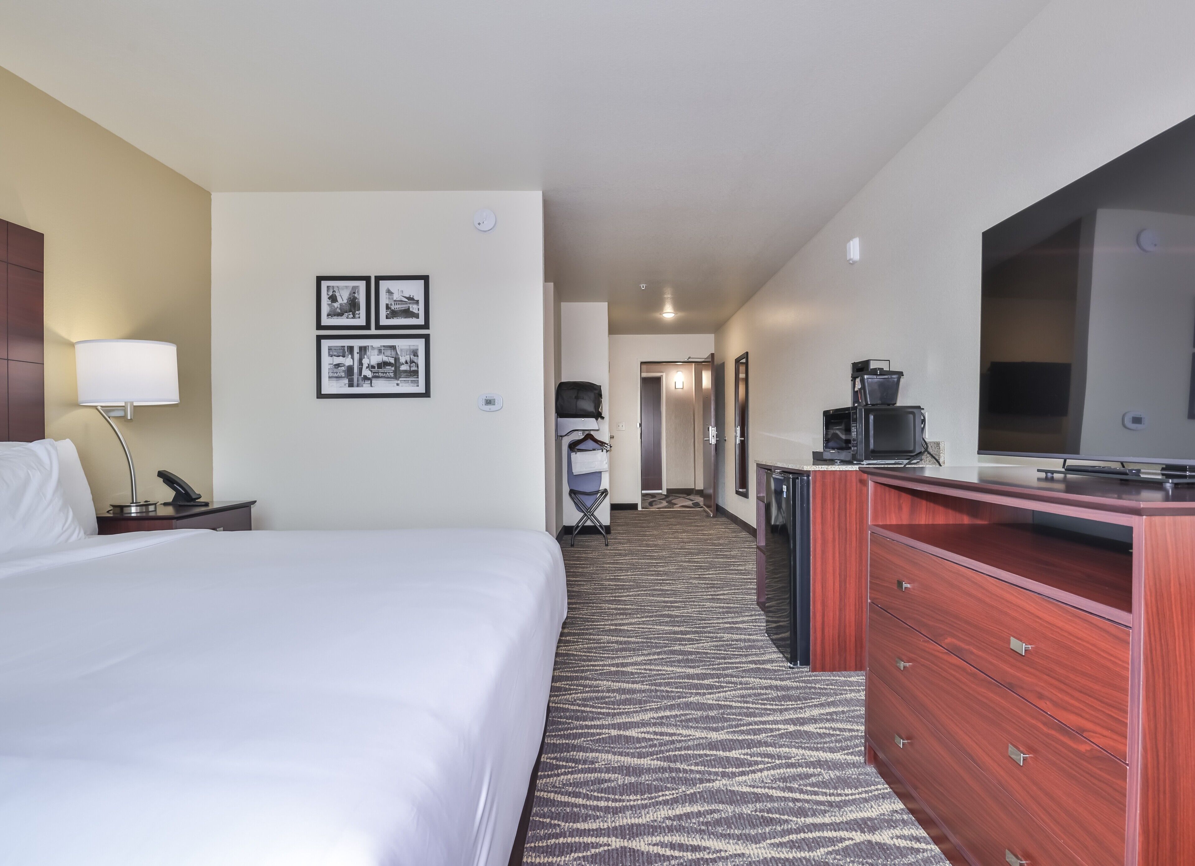 Quarto de hotel com cama, escrivaninha com luminária, cômoda, televisão e micro-ondas.