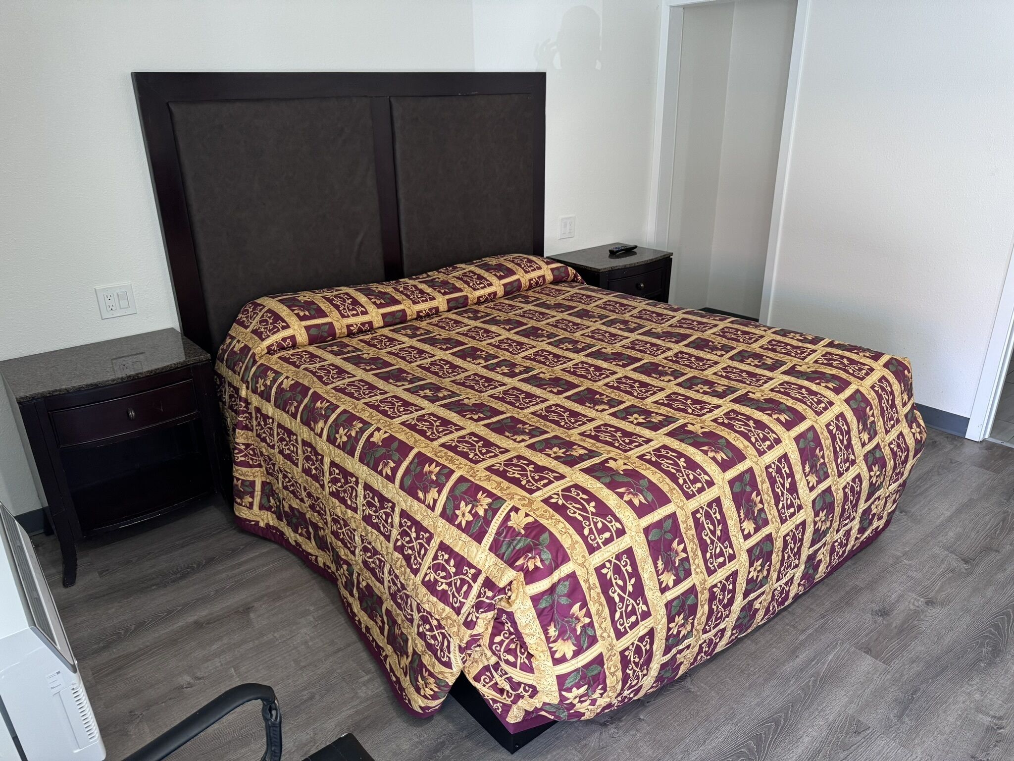 Uma cama bem arrumada com colcha estampada, cabeceira escura e duas mesas de cabeceira.