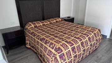 Uma cama bem arrumada com colcha estampada, cabeceira escura e duas mesas de cabeceira.