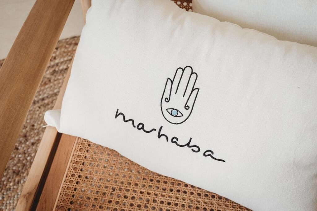 Almofada branca com marca de mão e a palavra 'mashaba' bordada.