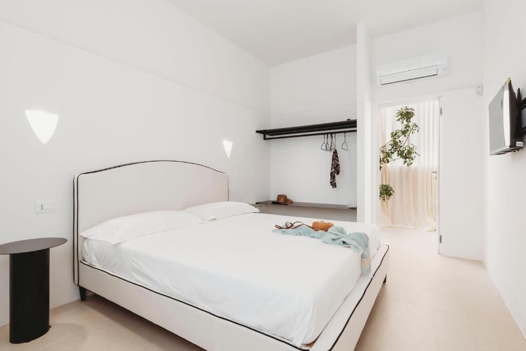 Quarto moderno com cama, mesa de cabeceira e televisão na parede.