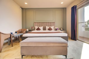 Quarto de hotel com cama grande, mesa de cabeceira, cadeira e vista para o exterior.