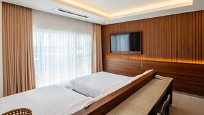 Quarto de hotel moderno com uma cama grande, uma televisão presa à parede e detalhe em painéis de madeira.