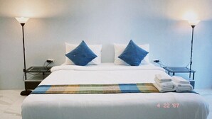 Quarto de hotel com uma cama bem arrumada, duas luminárias de cabeceira, uma mesinha com abajur e uma toalha dobrada na cama.