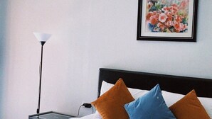 Uma cama bem arrumada com lençóis brancos, um travesseiro azul e castanho, e uma toalha dobrada ao lado.