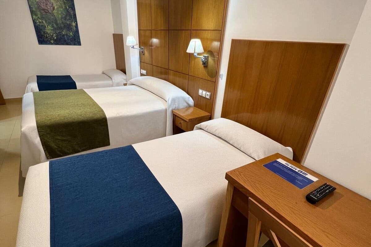 Quarto de hotel com duas camas, uma escrivaninha, uma luminária e um quadro na parede.