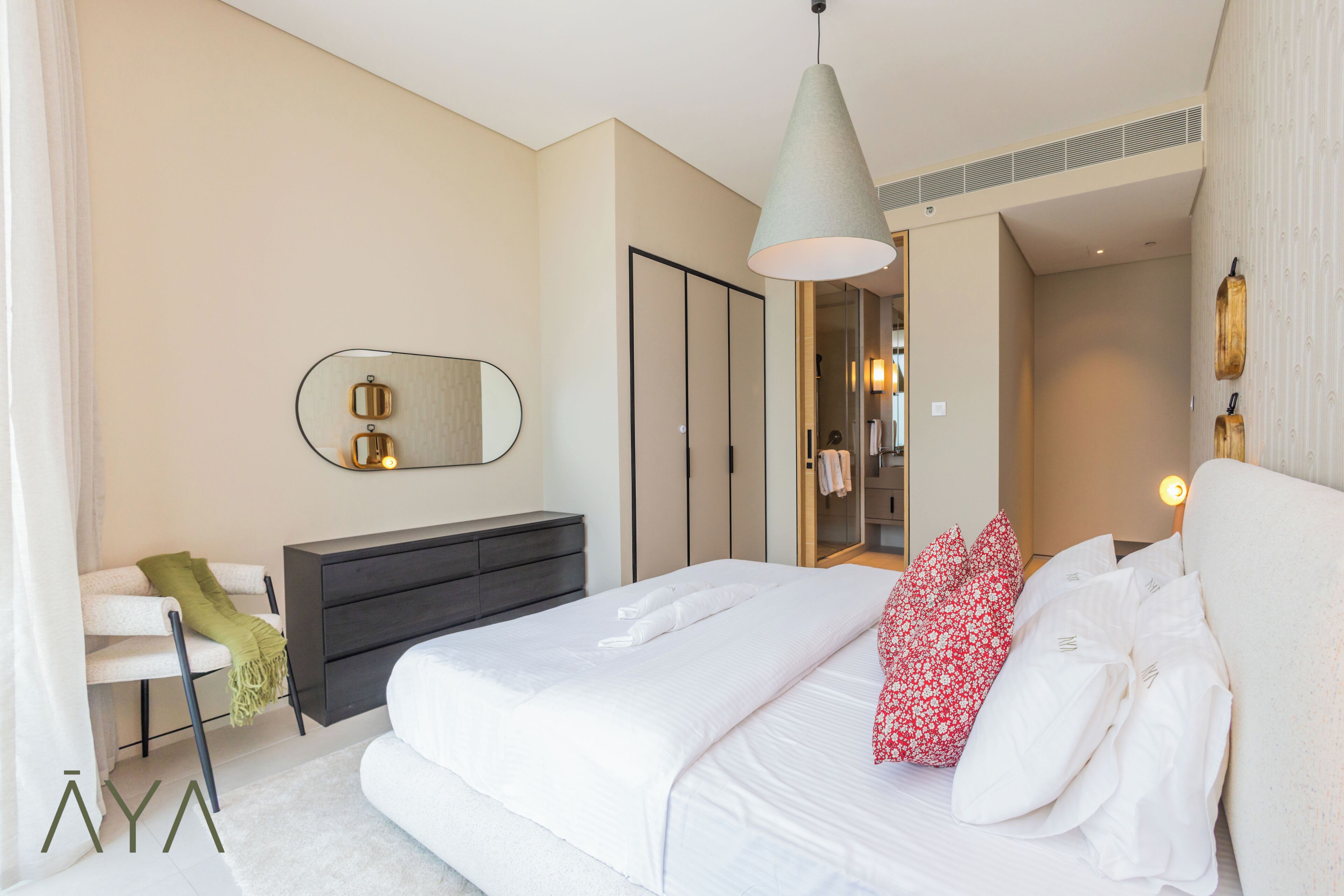 Quarto moderno com uma cama grande, cômoda, espelho e luminária suspensa.