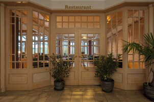 Entrada de restaurante com portas duplas, plantas em vasos e piso de azulejos.