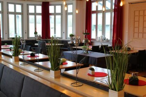 Restaurante com mesas compridas, detalhes em vermelho e plantas em vasos.