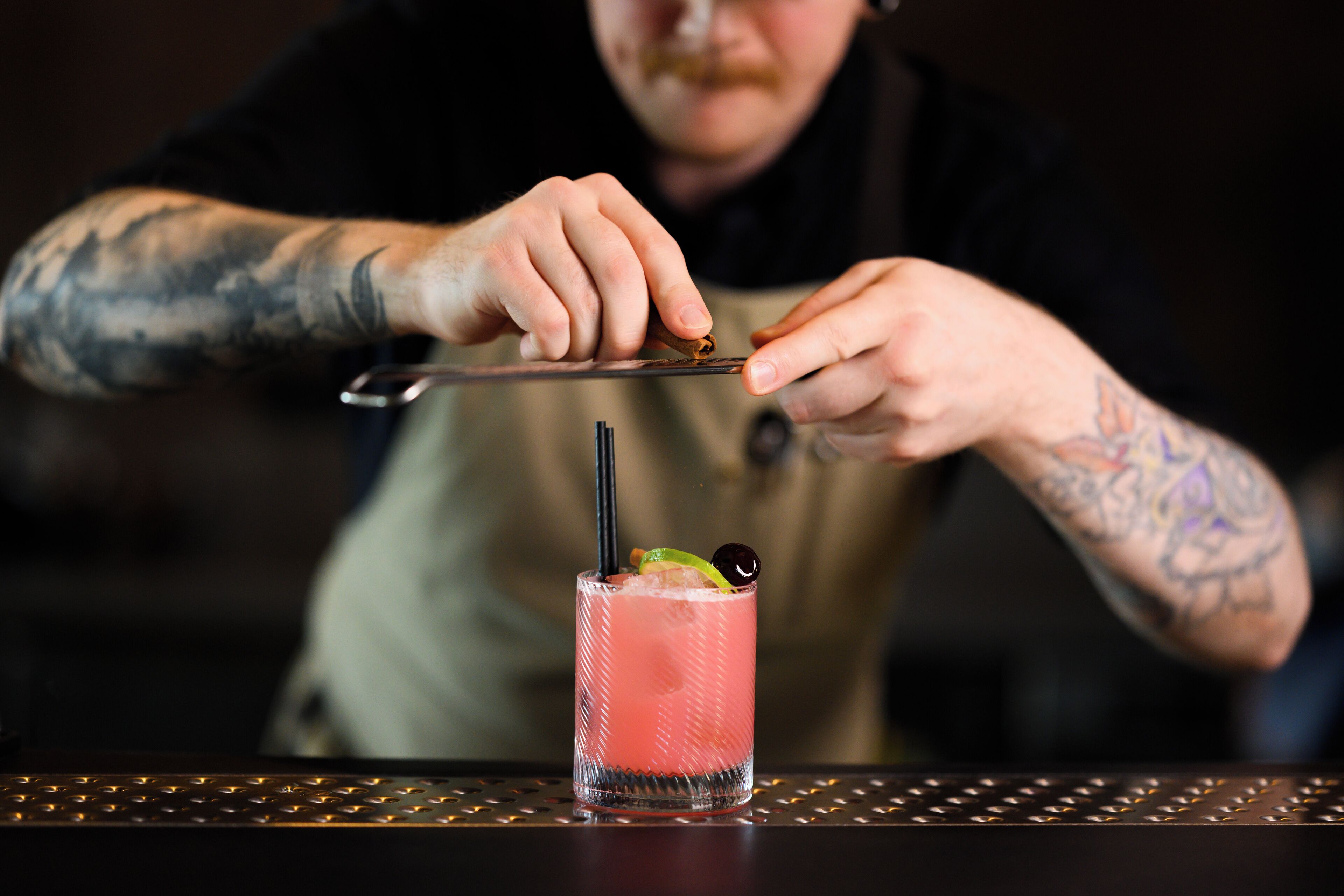 Um bartender prepara uma bebida com um coqueteleira e um copo no balcão do bar.