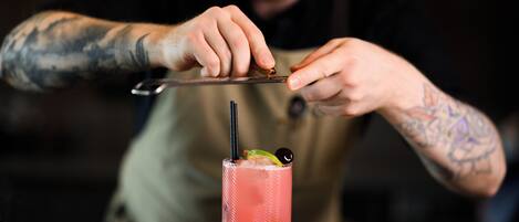 Um bartender prepara uma bebida com um coqueteleira e um copo no balcão do bar.