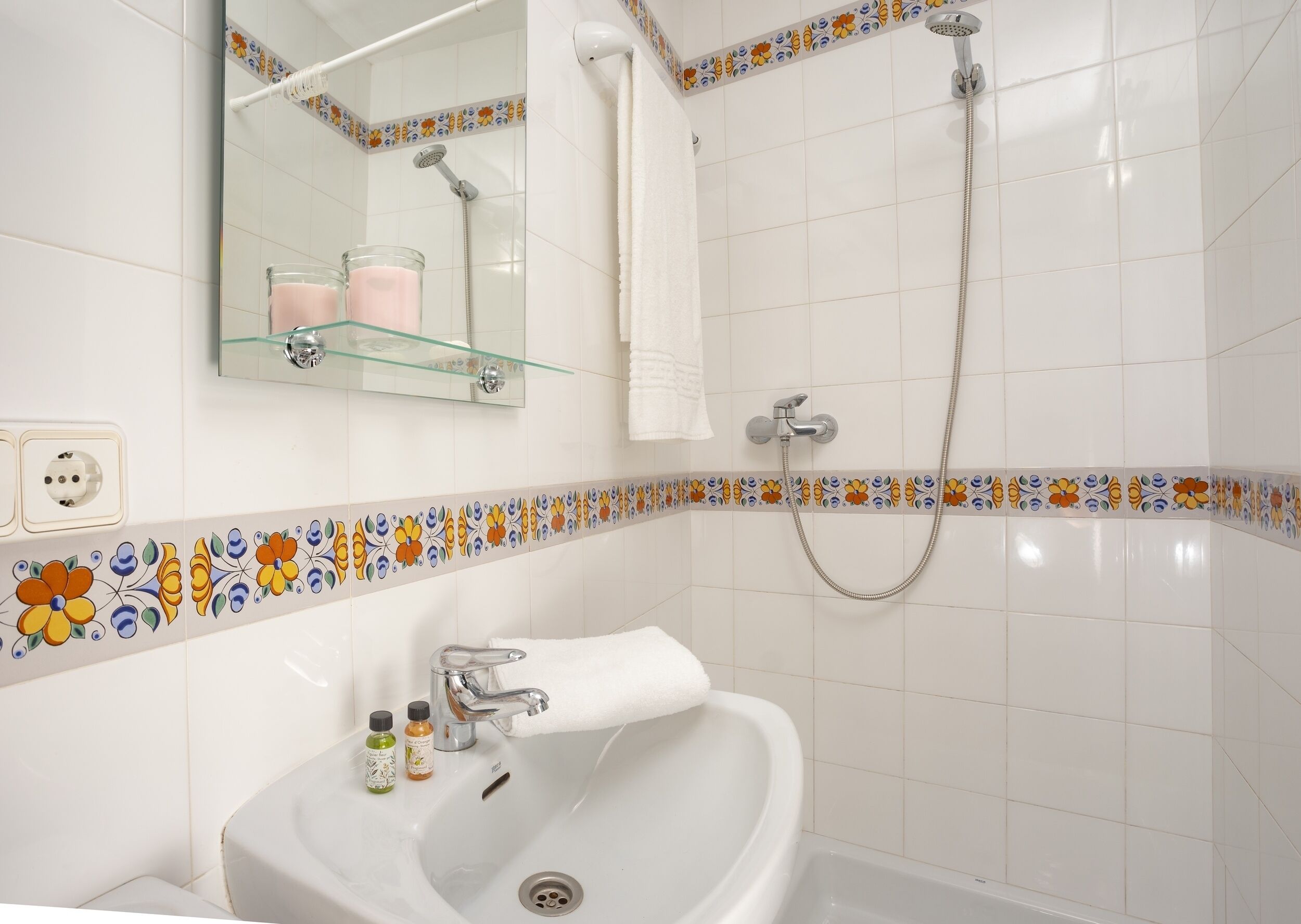 Casa de banho com lavatório, espelho, chuveiro e azulejos decorativos.