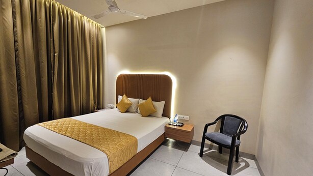 Quarto de hotel com uma cama grande, uma mesa de cabeceira, uma cadeira e um ventilador de teto.