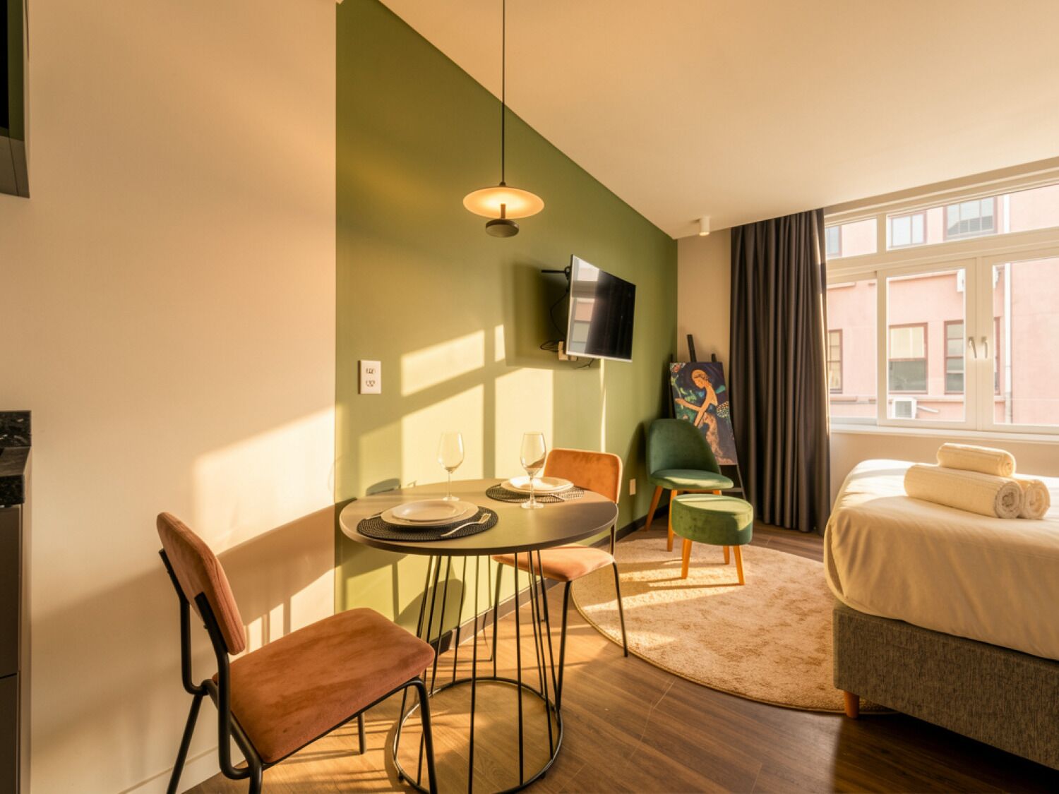 Quarto de hotel com mesa de jantar, cadeiras, uma cama, televisão e um quadro na parede.