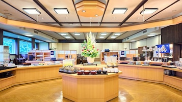 Um saguão de hotel com um balcão de recepção central, um grande arranjo floral e uma área de buffet com diversos alimentos.
