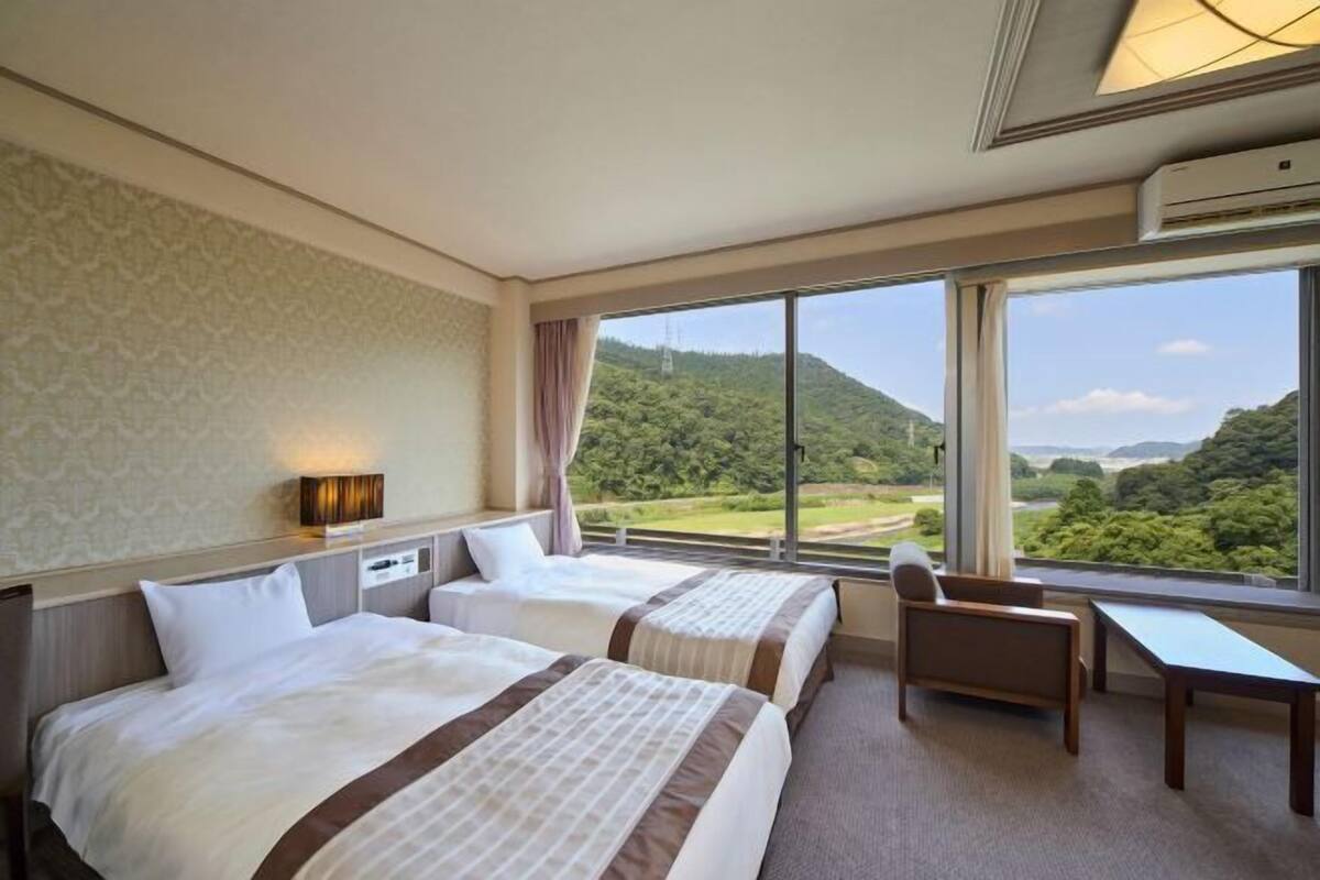 Quarto de hotel com duas camas, uma escrivaninha e uma cadeira.