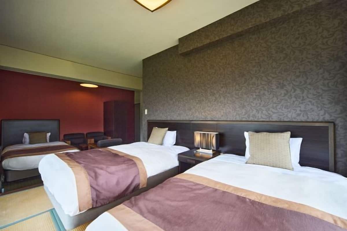 Quarto de hotel com duas camas, uma janela grande e piso coberto por carpete.