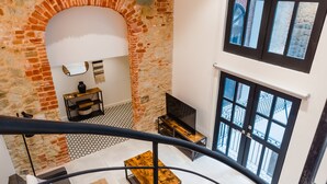 Escadaria em espiral com parede de pedra e vista para uma sala de estar com lareira.