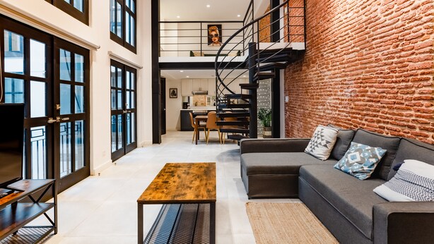 Uma sala de estar espaçosa com um sofá moderno, uma mesa de centro de madeira e uma escada que leva a um andar superior.