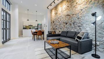 Uma sala moderna com uma parede de destaque em pedra, um sofá cinza, uma mesa de centro de madeira e uma área de jantar com mesa e cadeiras brancas.