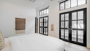 Quarto com uma cama grande, ventilador de teto e várias janelas.