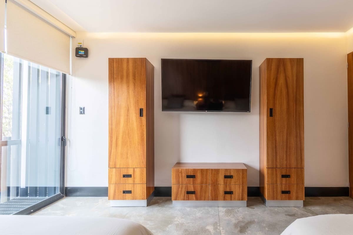 Quarto moderno com televisão de tela plana na parede, armários de madeira com gavetas e porta de vidro deslizante.