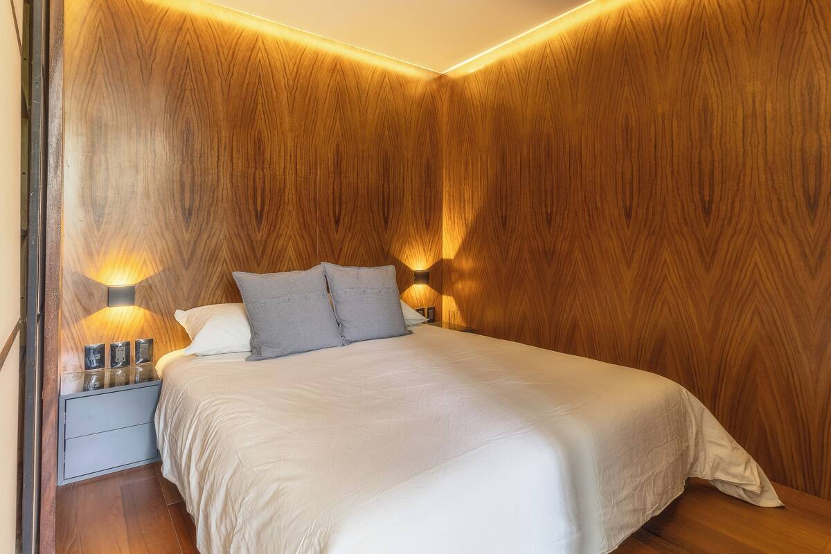 Quarto com parede de madeira, cama com roupa de cama branca e duas luminárias de cabeceira.