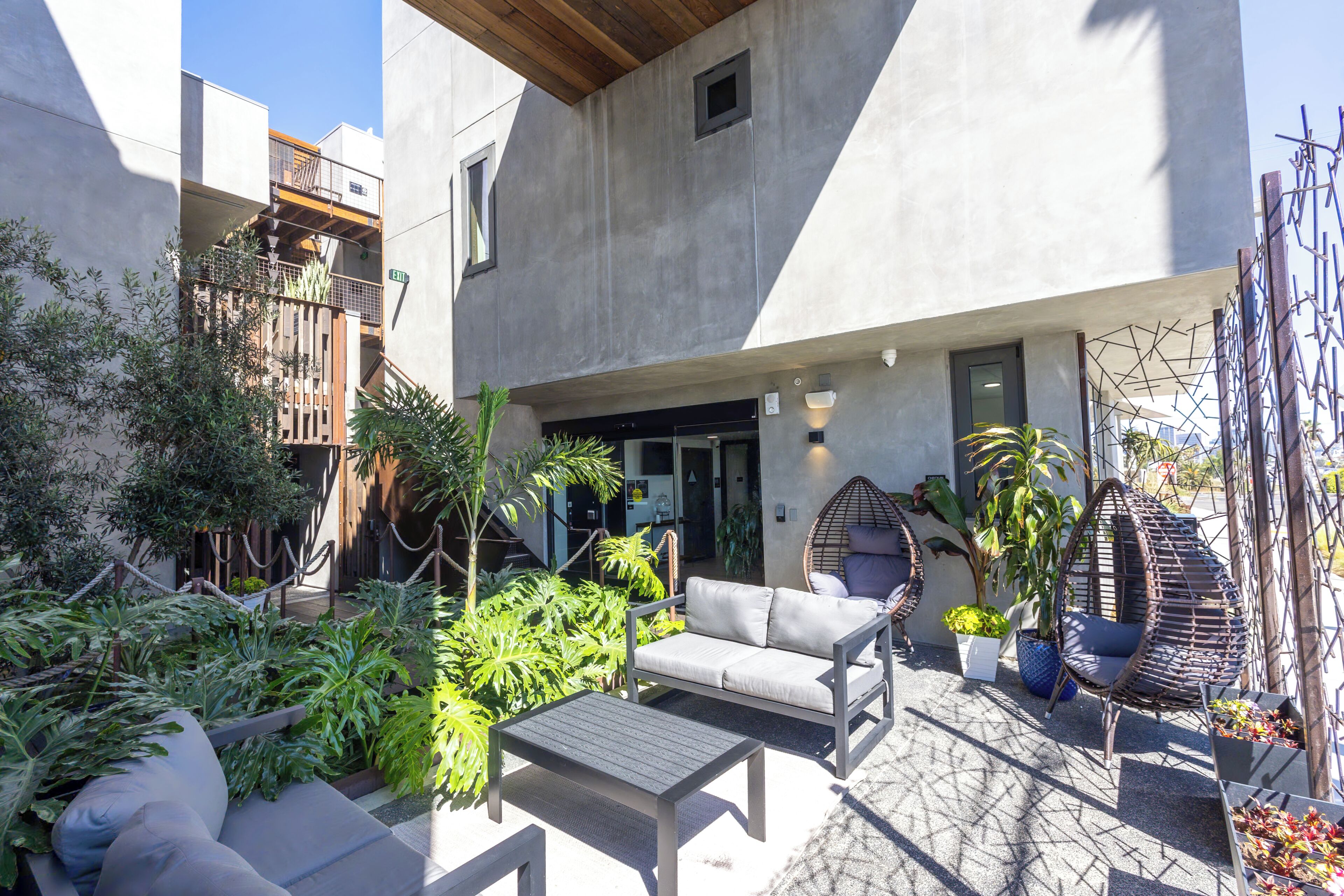 Um pátio ao ar livre com sofá, mesa e cadeiras, rodeado por plantas e um cercado de madeira.