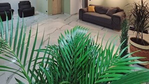 Uma sala de estar ampla com piso de mármore, um sofá, duas poltronas e uma porta de madeira.