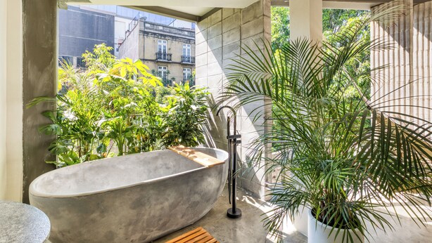 Uma casa de banho moderna com uma banheira independente, uma planta em vaso e vista para a cidade.