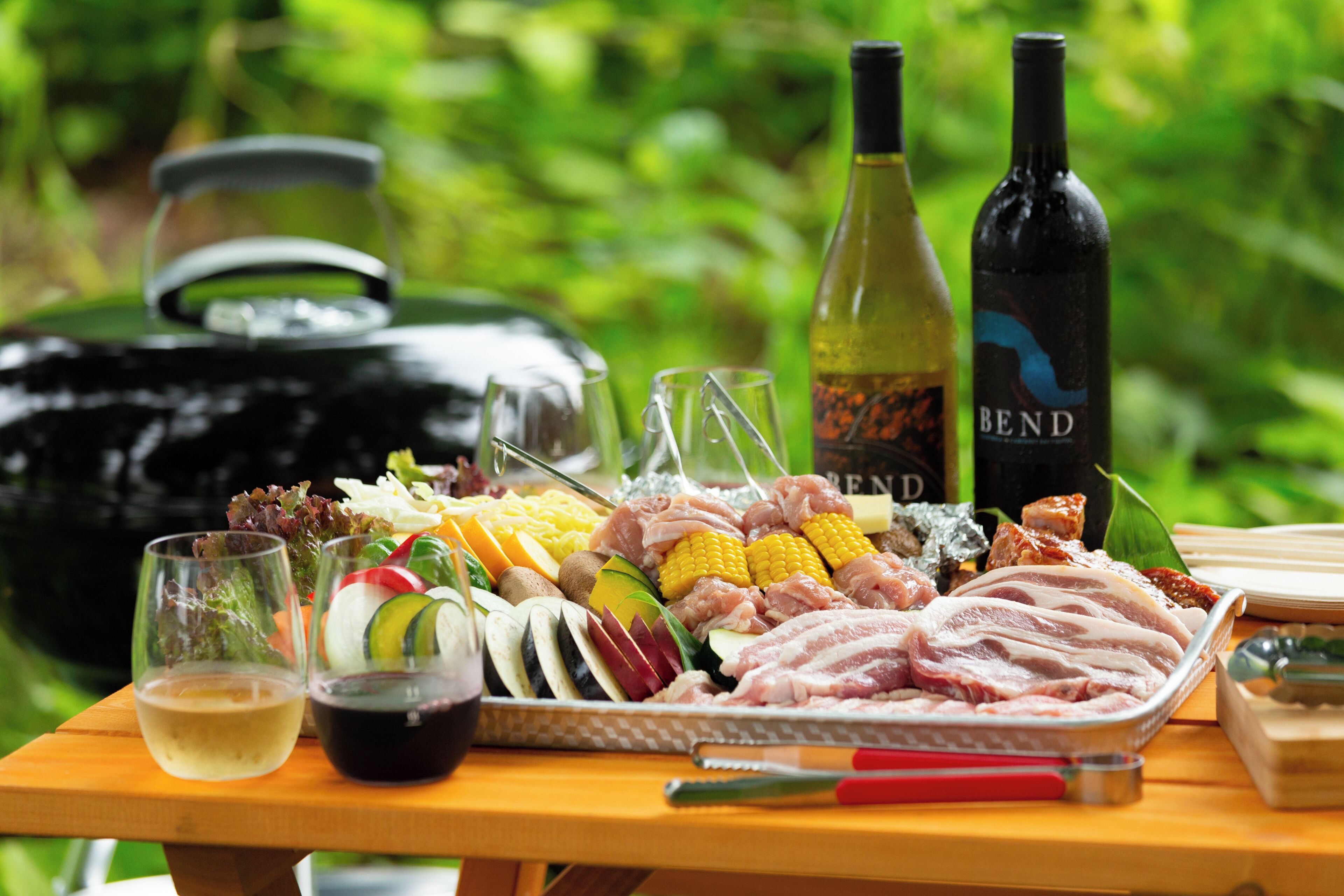 Um piquenique com diversos alimentos, bebidas e uma garrafa de vinho sobre uma mesa de madeira.
